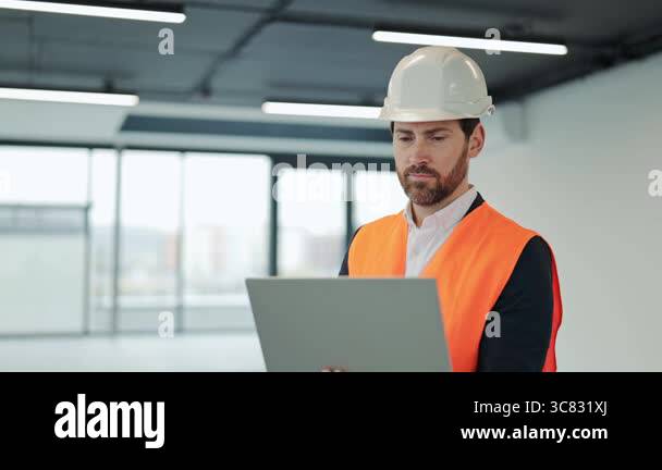 Successful engineer in an orange vest and a white helmet works on a ...