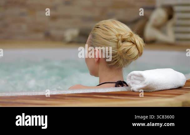 A serene back view of a young woman reclining in a bubbling jacuzzi ...