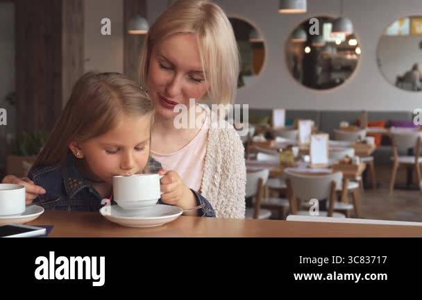 A charming little girl sips tea from a delicate white cup while her ...