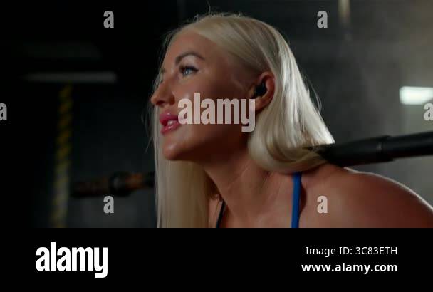 In a modern gym a woman with long light hair focuses on her form as she ...