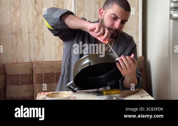 Man fixing frying pan with screwdriver while sitting in old kitchen ...