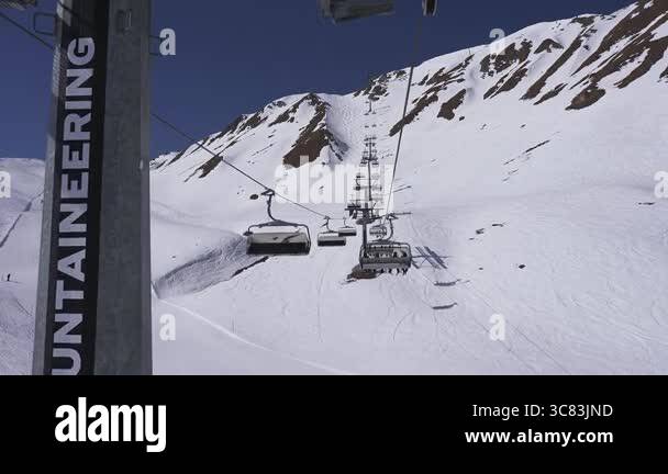 A ski lift moves upward on a snowy mountain slope in the Alps, with ...