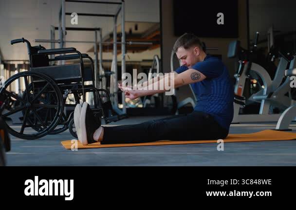 Athletic man performs seated forward stretch on yoga mat in a gym ...
