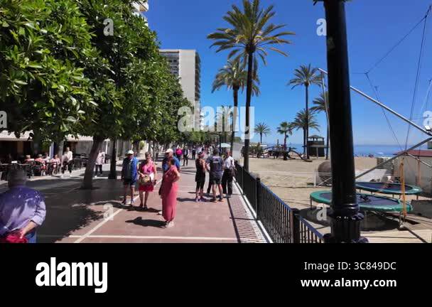 People strolling along the seafront promenade in Marbella, Spain, with ...