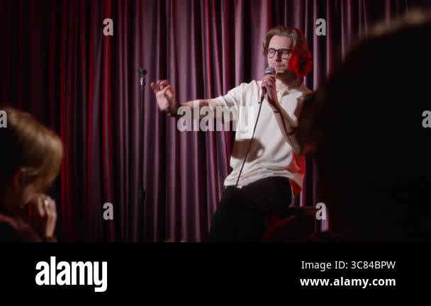 Young man in glasses giving stand-up performance on stage, talking in ...