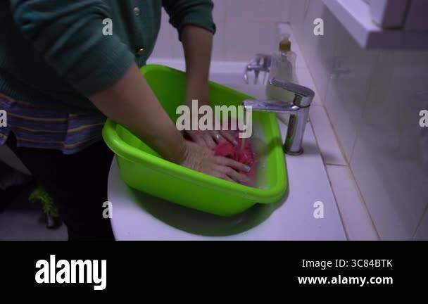 Rinse clothes in water under the tap. Hand washing in a green basin ...