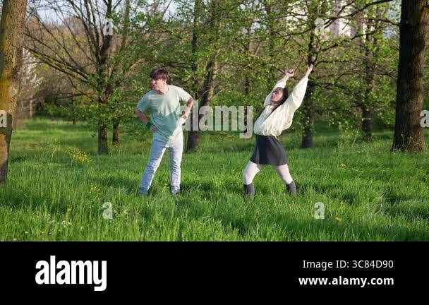 Two friends joyfully dance together in a lush green park during spring ...
