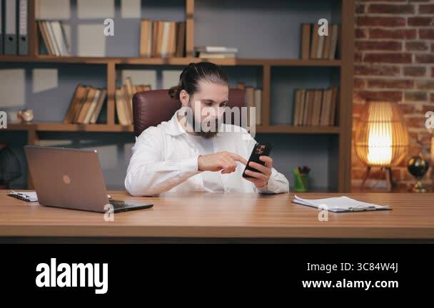 Bored Caucasian man with neat beard tapping on smartphone while sitting ...
