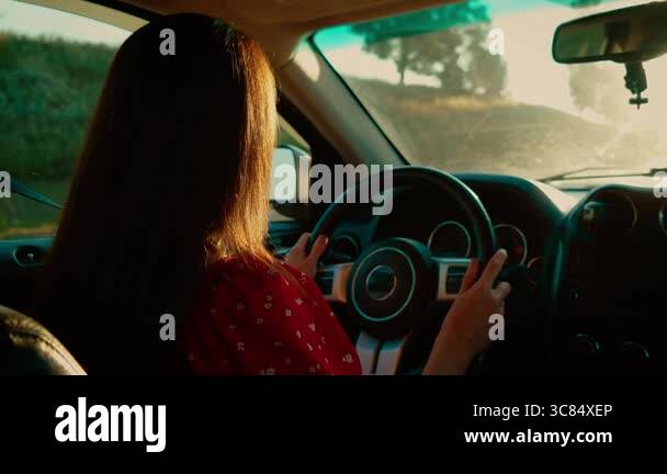 Young woman in red dress driving car, holding steering wheel with ...