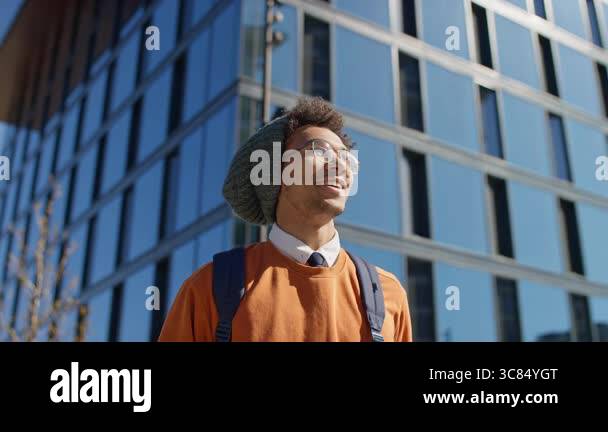 Happy young man with backpack and casual outfit smiling while walking ...