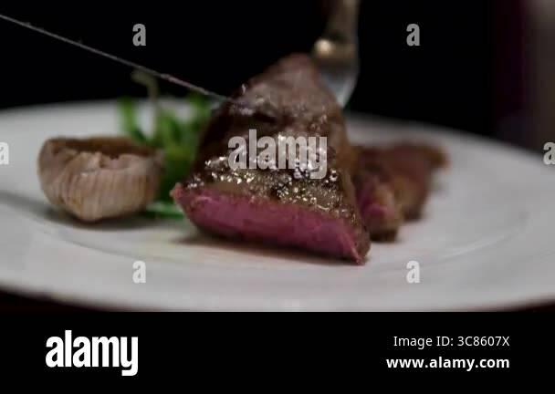 Chef slicing freshly grilled juicy beef steak meat with a knife on a ...