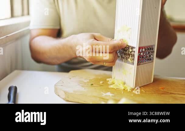 Chef grating vegetables using a manual grater on a wooden cutting board ...
