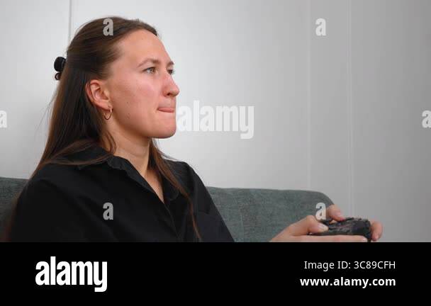 Young woman sitting on comfortable sofa, intensely playing videogame ...
