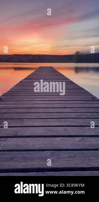 Wooden pier stretching into a calm lake at colorful sunset. Peaceful ...