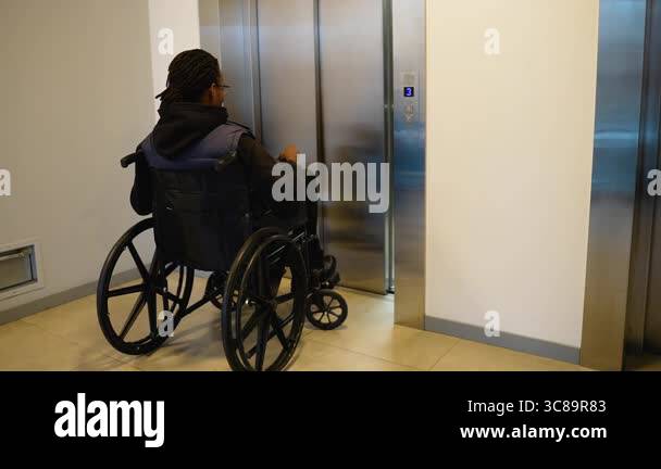 Man in wheelchair approaching elevator in accessible building ...
