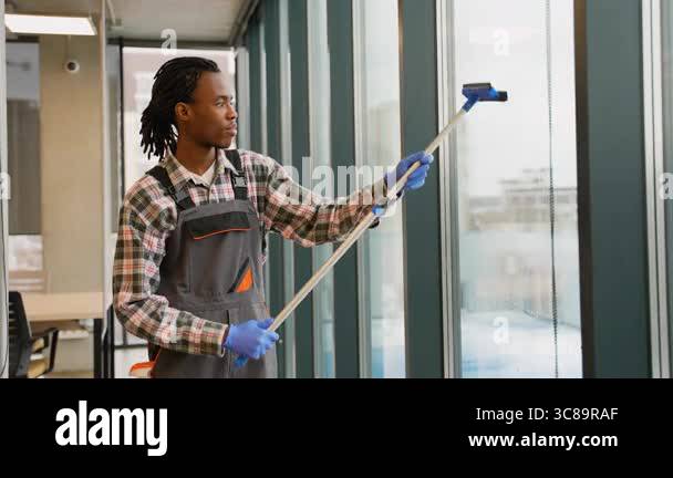 Professional African American cleaner wearing gloves and overalls using ...
