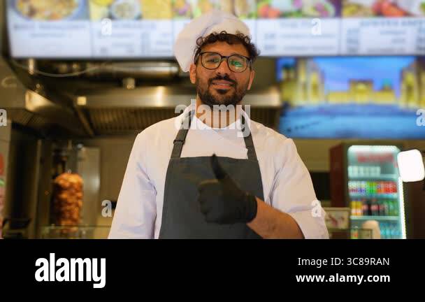 Smiling Middle Eastern chef in uniform and apron showing thumbs up ...
