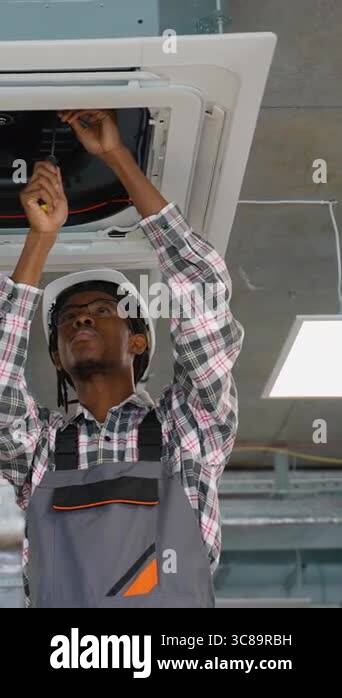 Professional HVAC technician in uniform and helmet repairs a ceiling ...