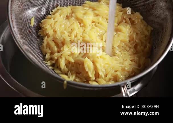 Close-up video of rinsing freshly cooked orzo pasta under running water ...