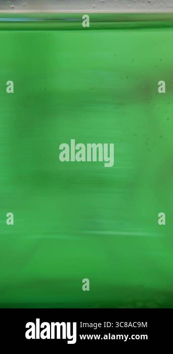 Vertical macro view of red drops being added to green liquid in flask ...