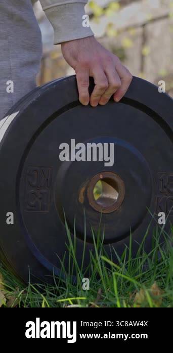 A person prepares to lift a weight plate in a grassy outdoor setting ...