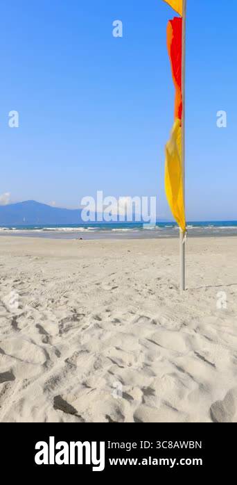 Outdoor summer beach scene with colorful flags, calm waves, and clear ...