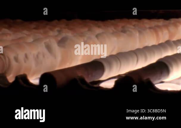 Rows of traditional Japanese pastry dough baking on rotating metal rods ...