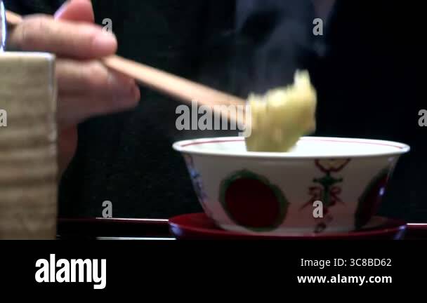 Hand using chopsticks to pick up steaming dumpling from ceramic bowl ...