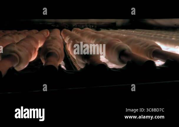 Close-up of pastry dough baking on rotating metal rods inside oven ...