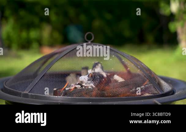 A metal fire pit with a mesh top. The fire is burning inside the pit ...