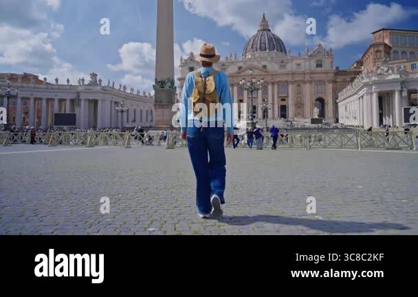 A girl tourist in a hat and with a backpack walks along as she admires ...
