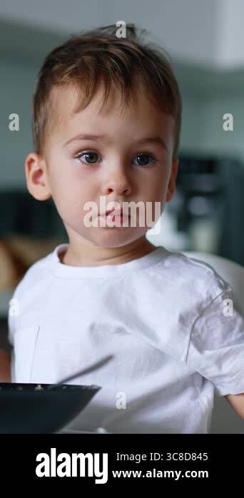 Focused baby boy looking ahead sits at table. Toddler holds a piece of ...