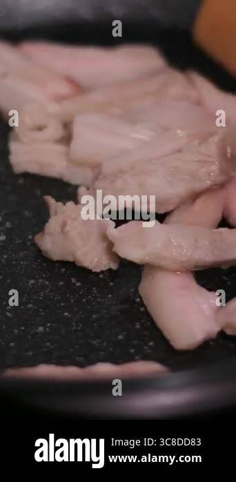 Putting salt and stirring over a fresh pork chop on frying pan . High ...