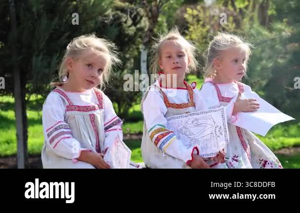 Three little girls, triplet sisters, are sitting on a bench, wearing ...
