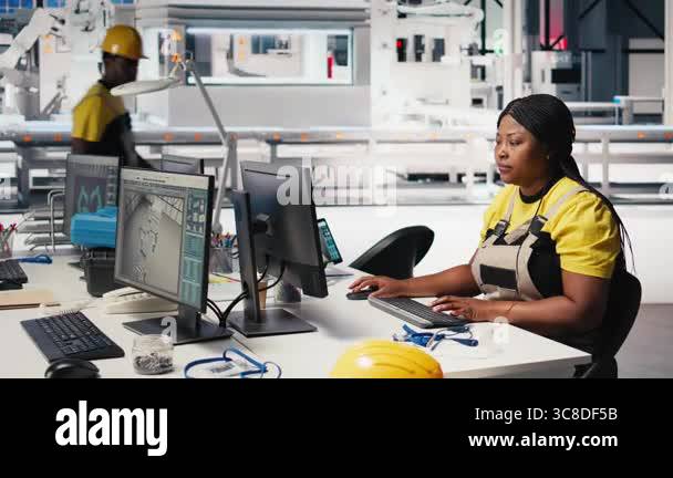Black factory employee oversees solar system performance at desk seated ...