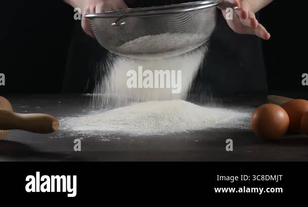 Woman sieving flour, making well and breaking egg into it at dark ...