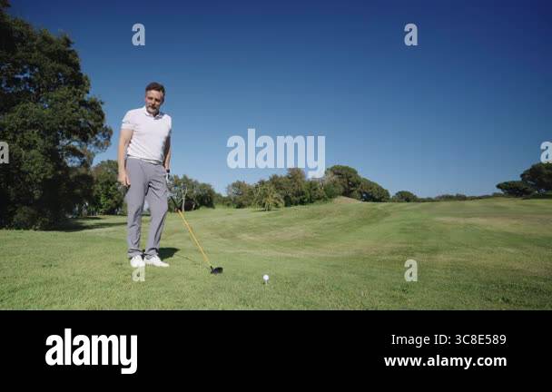 Professional golfer driving golf ball on lush green course under bright summer sunlight ...