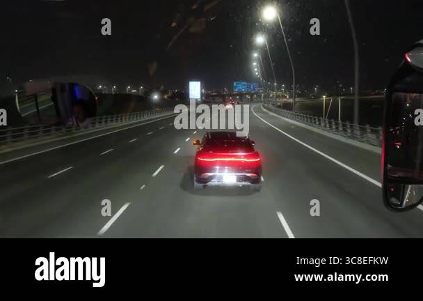 A red car speeds on a deserted highway at night, headlights ...