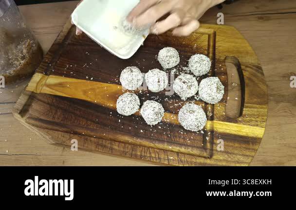 Hands are rolling mixture into bite-sized energy balls and coating them ...