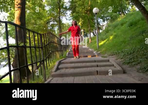 An elderly woman in red clothes walks in the park. She walks down a ...