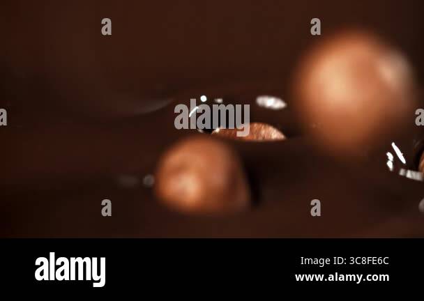 The hazelnuts fall into the liquid chocolate. Filmed on a high-speed ...