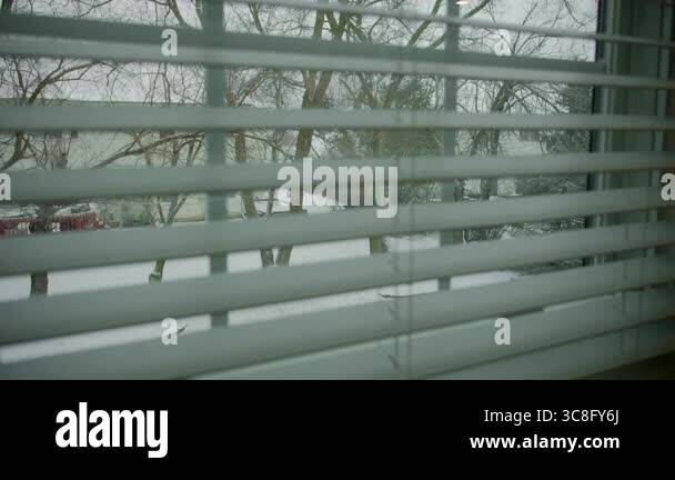 View from house inside at winter street through window with blinds ...