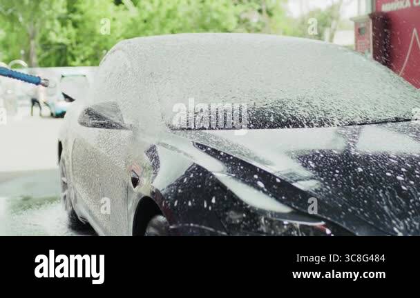 A car is thoroughly covered with thick foam during an outdoor car wash ...