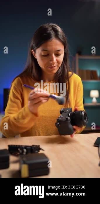 Woman photographer cleans camera dust with special brush sitting home ...