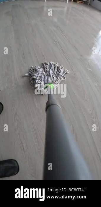 POV closeup of man mopping wooden floor at home from above, showing ...