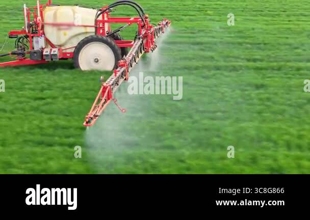 Close-up of a farmer spraying crop field with red machinery sprayer ...