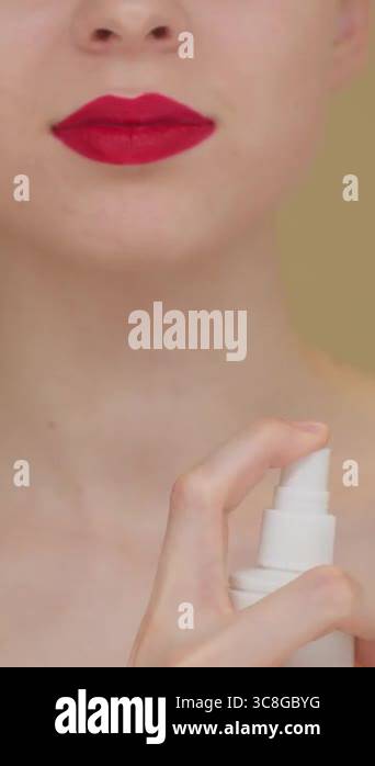 VERTICAL VIDEO: Closeup of a woman spraying a hydrating mist on her ...