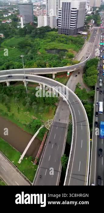High-angle view of highway traffic, flyover, city buildings, and lush ...