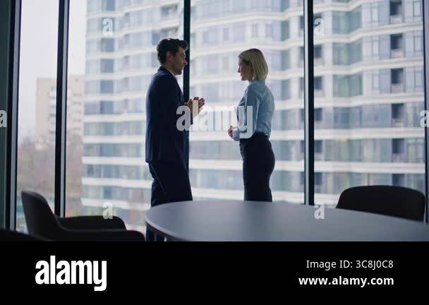 Corporate partners speaking by office panoramic window. Smiling ...
