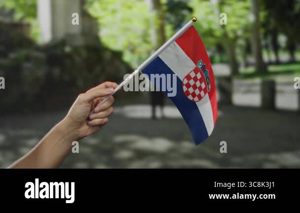 Hand holding croatian flag outdoors in city street with greenery ...